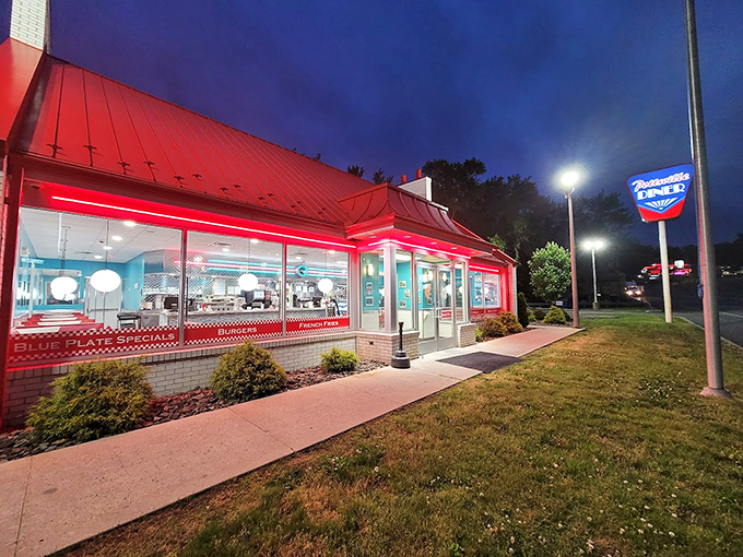 As night falls, the diner glows like a red-roofed lighthouse guiding hungry souls to safe harbor. Those windows promise warmth inside.