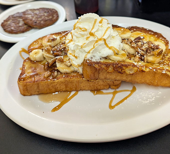 French toast elevated to art form - caramelized bananas, whipped cream, and syrup creating a breakfast that feels like getting away with dessert before noon.