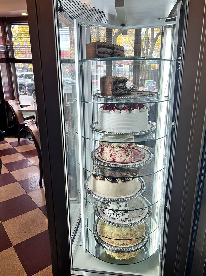 The rotating cake display&mdash;a glass tower of temptation where willpower goes to die and "I'll just have a bite" becomes a beautiful lie.