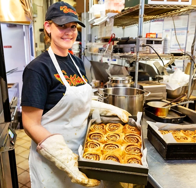 Behind the scenes, fresh trays of cinnamon magic emerge from skilled hands. The artist and her masterpieces, ready to make someone's day.