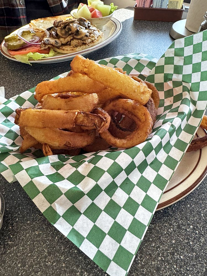 Onion rings wearing their golden batter coats with pride, stacked like delicious jewelry on a checkered green backdrop of diner authenticity.