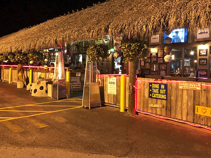 As night falls, the tiki bar transforms into a beacon for seafood pilgrims. The palm-thatched exterior glows with promise of fresh catches and cold drinks.