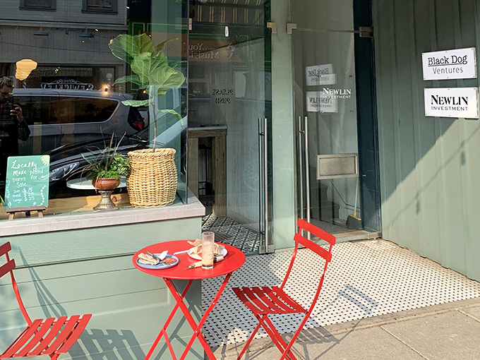 Sidewalk seating that transforms an ordinary Tuesday into a Parisian holiday. Red chairs against sage green &ndash; a color combination that somehow makes coffee taste better.