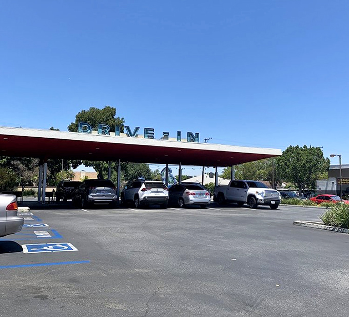 The drive-in canopy stands like a mid-century modern cathedral. Cars gather beneath it in reverent anticipation of burgers delivered car-side.