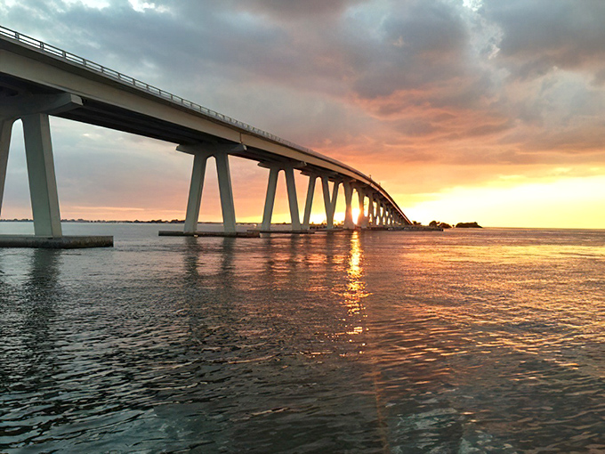 The bridge's silhouette against a fiery sunset sky creates the kind of moment that makes you pull over, grab your phone, and try&mdash;futilely&mdash;to capture pure magic.