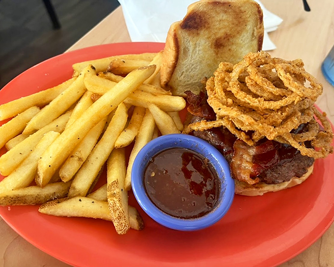 A burger that demands to be eaten with both hands, accompanied by golden fries and crispy onion rings that crunch loud enough to turn heads. 