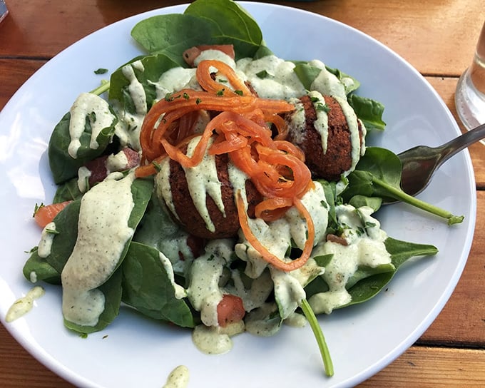 A garden on a plate: vibrant spinach leaves cradle perfectly fried falafel balls, drizzled with herb-flecked dressing and topped with carrot ribbons.