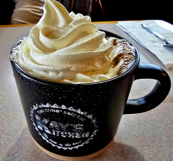 Hot cocoa topped with whipped cream towers arrives in a branded mug, delivering childhood comfort in adult-sized portions.
