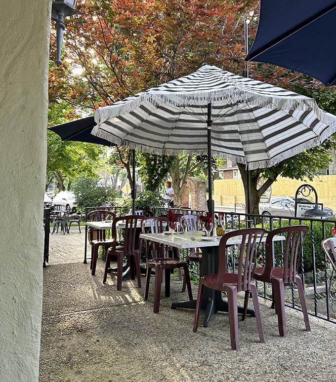 The outdoor seating area offers a casual European vibe where even plastic chairs feel sophisticated under striped umbrellas and dappled sunlight.