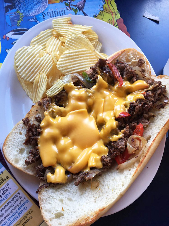 The Philly cheesesteak in its natural habitat—surrounded by rippled potato chips and draped in cheese sauce that defies the laws of physics.