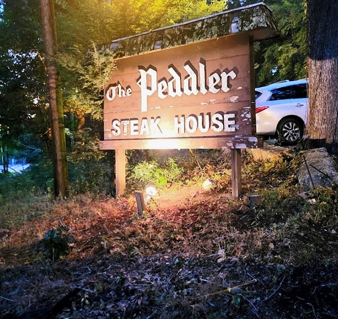 The wooden sign stands sentinel at dusk, illuminated like a beacon guiding hungry travelers to their reward.