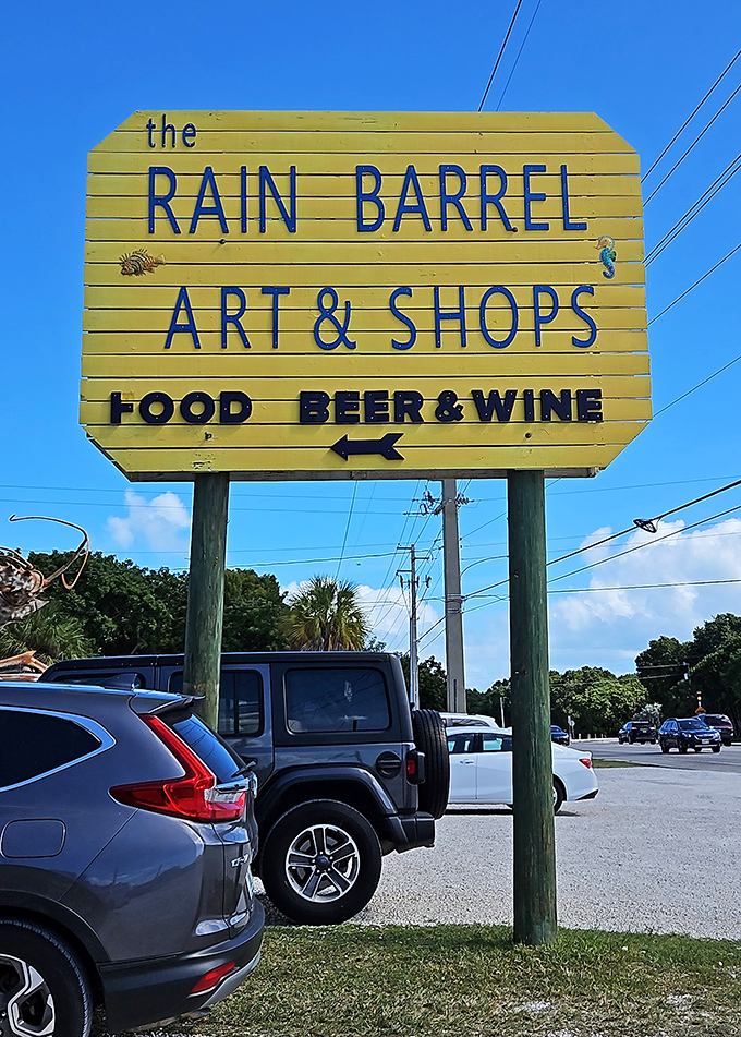 The yellow roadside sign makes a simple but important promise&mdash;art, shopping, and refreshments await just beyond the palm trees.