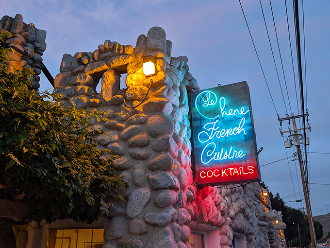 As twilight falls, the neon sign glows like a lighthouse, guiding hungry travelers to this stone-walled sanctuary of French cuisine.