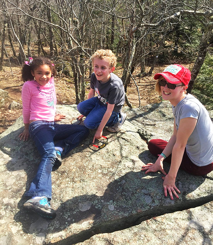 The image shows visitors enjoying the natural rock formations at the park. The joy of discovery is written across their faces as they explore the geological wonders of Pawtuckaway.