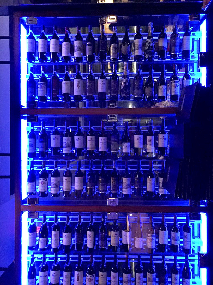 The wine display glows with an otherworldly blue light, showcasing bottles that range from "Tuesday night dinner" to "celebrating that inheritance from Uncle Bob."