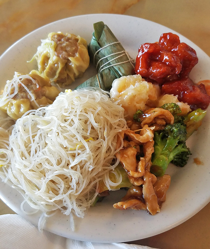 A perfect buffet plate balances delicate rice noodles, savory meat with broccoli, dumplings, and that mysterious leaf-wrapped treat you're definitely trying.