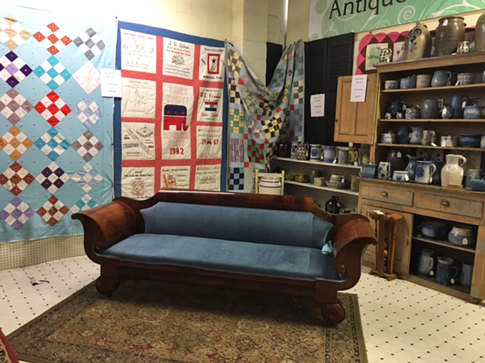 A Victorian-era fainting couch surrounded by handmade quilts – perfect for dramatically collapsing after realizing you've spent your entire afternoon treasure hunting.