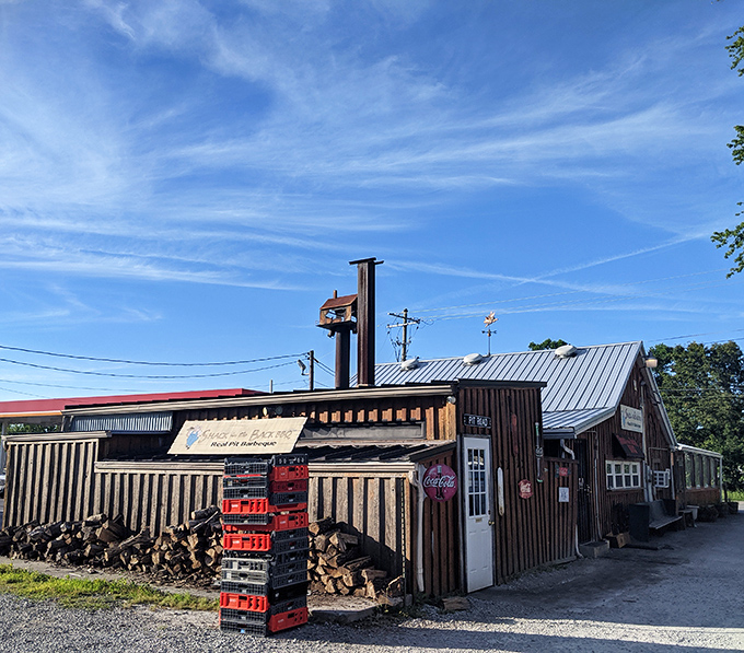 The smokehouse in its natural environment, with stacked wood nearby&mdash;visual evidence that proper barbecue isn't born in an electric oven.