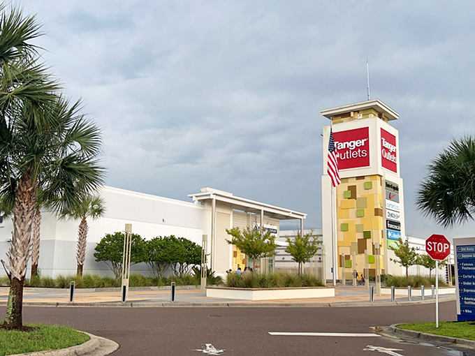 The iconic Tanger Outlets tower stands against moody Florida skies, a beacon calling to shoppers like a lighthouse guides sailors to shore.