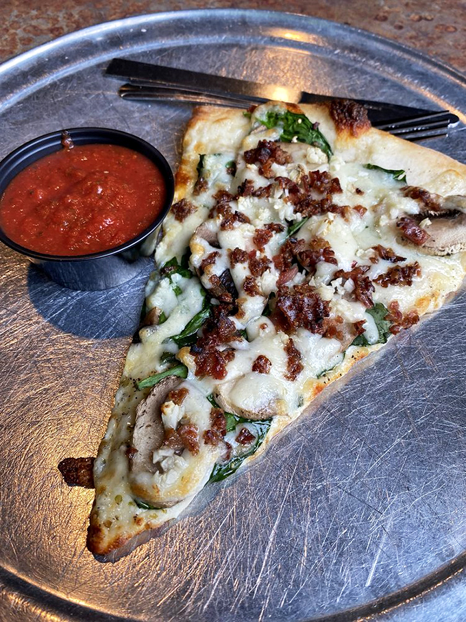 This slice showcases the kitchen's philosophy: quality ingredients arranged with care, where mushrooms, spinach and bacon create a harmonious trio.