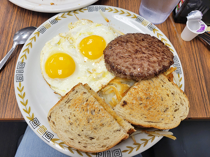 The breakfast trinity: perfectly cooked eggs, a juicy sausage patty, and toast ready for butter. Simple pleasures on a patterned plate.