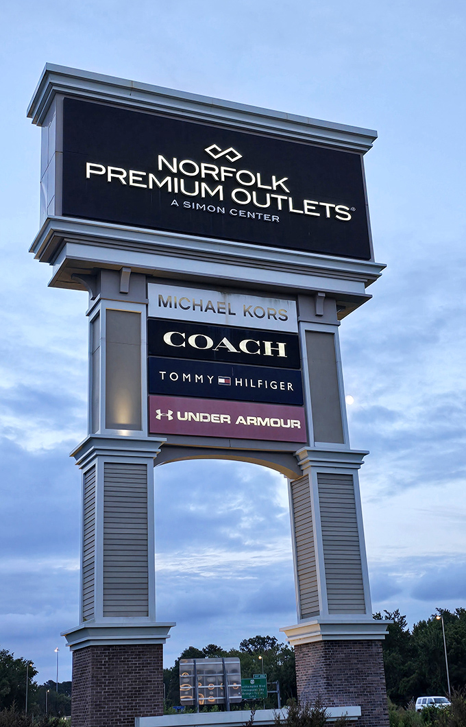 The towering entrance sign stands like a retail lighthouse, guiding discount-seeking shoppers to the promised land of premium brands.