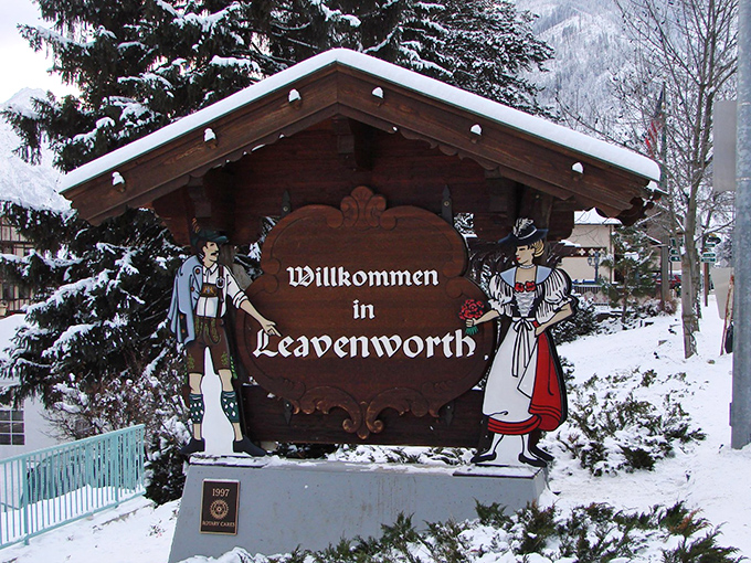 Snow dusts the "Willkommen in Leavenworth" sign and its wooden Bavarian figures, creating a winter greeting card that practically whispers "hot chocolate time."