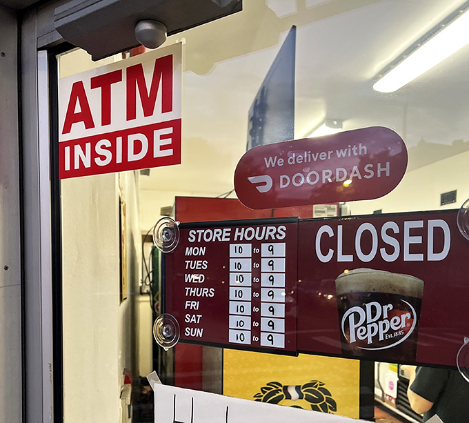 The door tells the whole story: ATM inside, DoorDash delivery, and hours that accommodate both early birds and night owls seeking sandwich salvation.