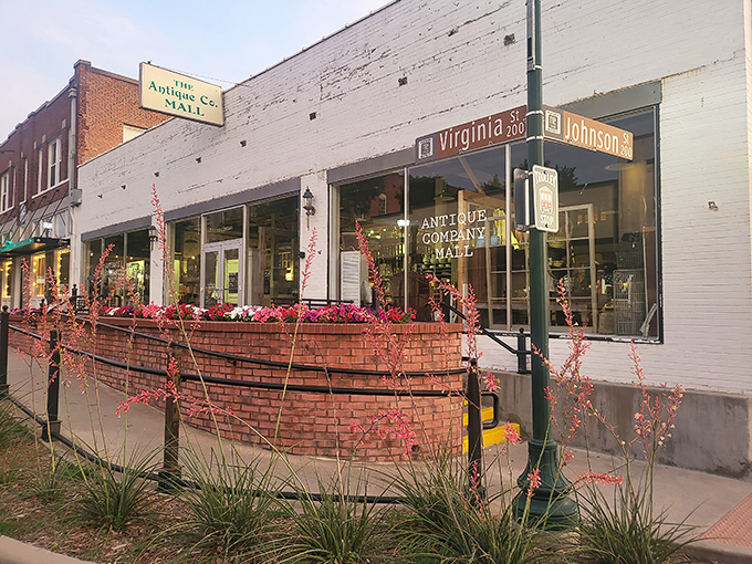 The Antique Company Mall's charming brick storefront welcomes treasure hunters with colorful flowers and vintage vibes.