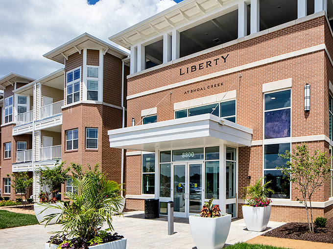 The welcoming entrance of Liberty at Shoal Creek, where beautiful flower pots add a splash of color to brick elegance.