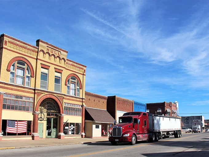 Truckin' through history! A crimson semi rolls past Neodesha's golden-bricked Hull building, where peace symbols and patriotism coexist like peanut butter and jelly.
