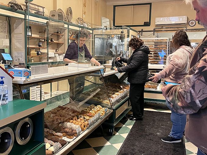 The classic green and white checkered floor sets the stage for donut drama, where patient customers wait for their sweet reward like game show contestants.