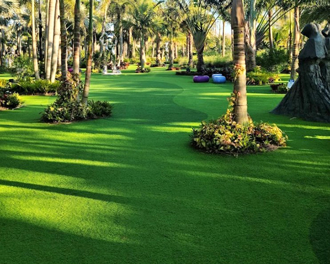Meticulously manicured emerald lawns create natural pathways between towering palms, inviting visitors to wander and discover artistic treasures around every corner.