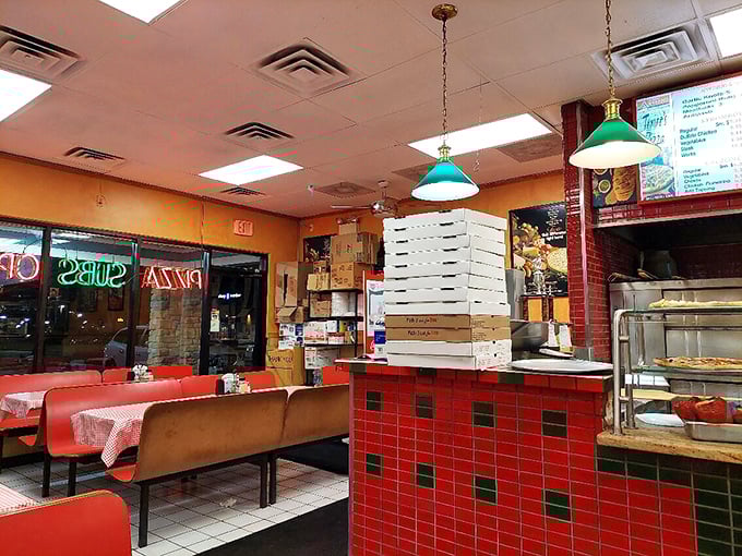 Classic pizzeria ambiance at its finest&mdash;red tile counter, stacked boxes, and green pendant lights creating that "you've arrived home" feeling every great pizza joint should have.
