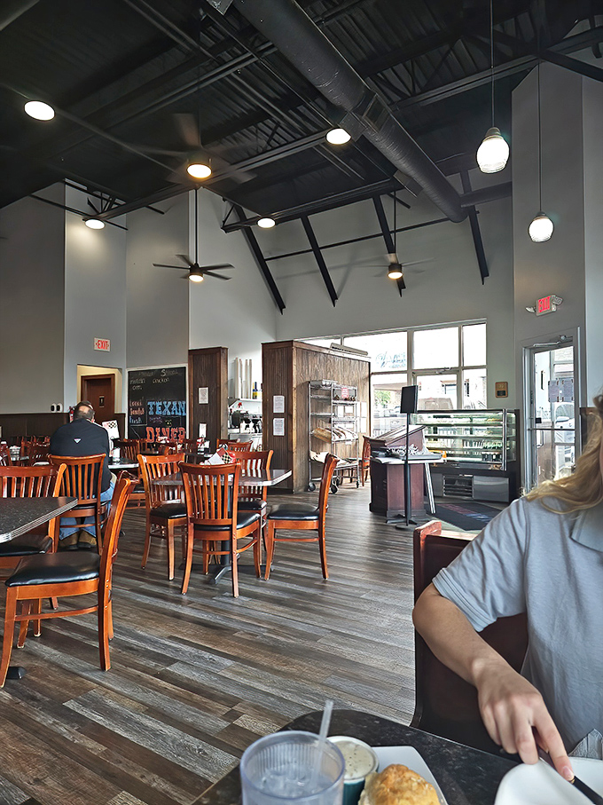 High ceilings, warm wood tones, and those cherry-colored chairs create the perfect backdrop for the comfort food drama about to unfold on your plate.