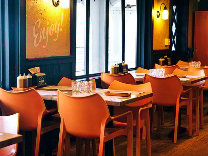 Inviting orange chairs and warm lighting create a cozy spot for you to enjoy a delicious meal with good friends.