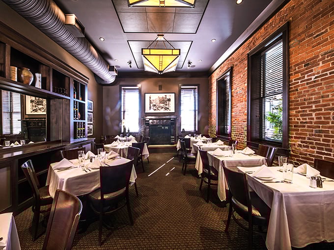 Exposed brick walls meet white tablecloths in this dining room where rustic charm and refinement find perfect harmony. That fireplace isn't just for show in winter!