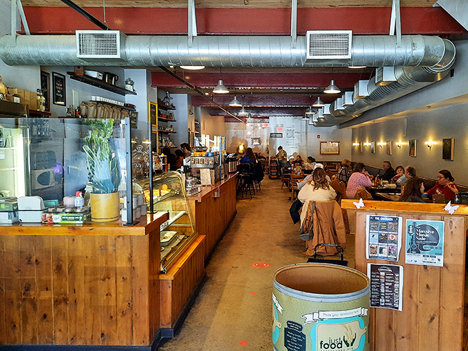 A narrow slice of breakfast heaven stretches before you, where exposed ductwork meets wooden warmth in a space that somehow feels both industrial and homey. 