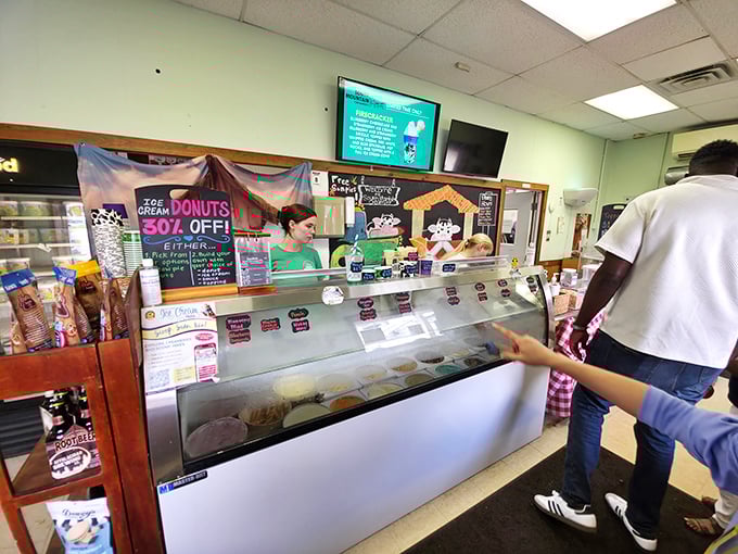Ice cream anticipation at its finest. The display case holds frozen treasures while a sign teases discounted donuts – because why choose just one treat?