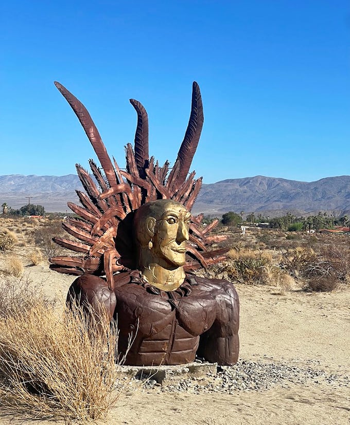 This majestic Native American warrior bust, complete with golden face and impressive headdress, stands sentinel over the desert landscape.