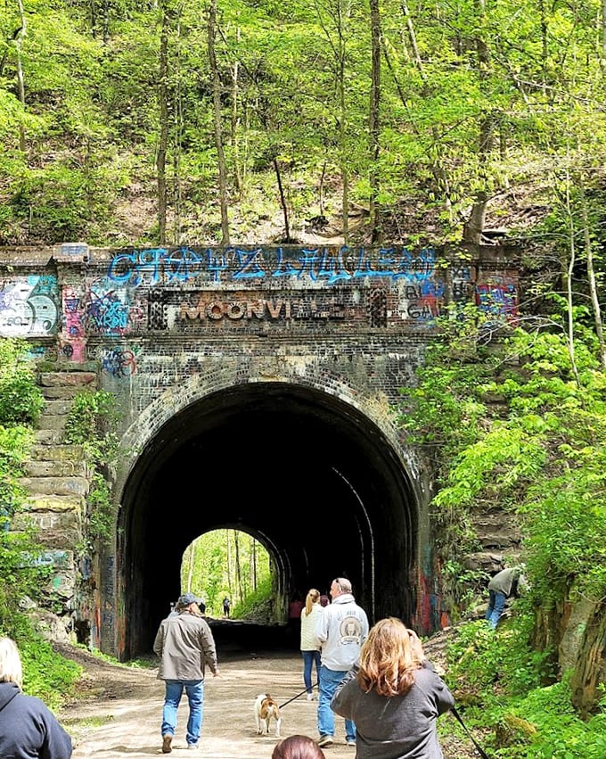 Spring brings vibrant greenery around the graffiti-adorned entrance, where visitors gather to experience this historic passageway that once connected forgotten communities.