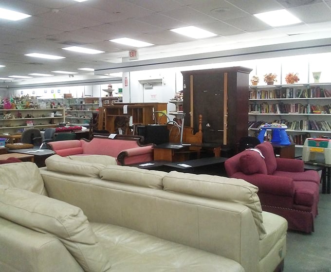 The furniture section resembles a living room showroom designed by a time-traveling decorator – cream sofas mingle with burgundy armchairs while vintage wooden wardrobes stand guard in the background.