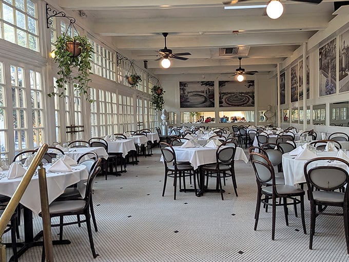 Sunlight streams through floor-to-ceiling windows, transforming this dining room into a bright sanctuary where white tablecloths await culinary treasures.