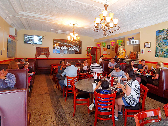 Red chairs and warm lighting create an inviting atmosphere where strangers become neighbors, united by their mutual appreciation for authentic Vietnamese cuisine.