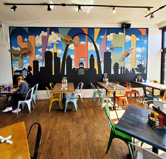 The vibrant mural featuring St. Louis' skyline and flying burgers sets the perfect backdrop for colorful metal chairs and wooden tables.