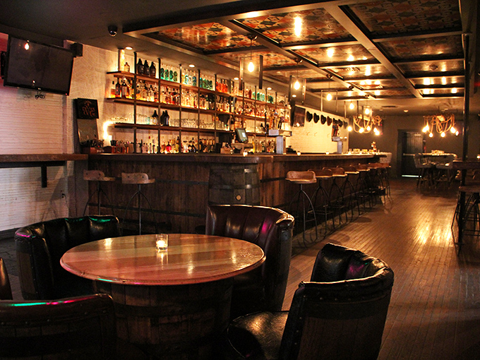 The bar at The Twisted Tail isn't just a bar – it's a bourbon library where wood, leather, and amber liquid create the perfect sanctuary.