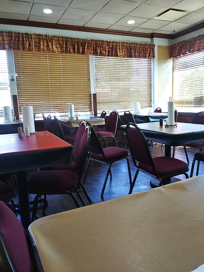 Simple tables, burgundy chairs, and plaid curtains create that "grandma's dining room" vibe where the only pretension is the expectation of clean plates.