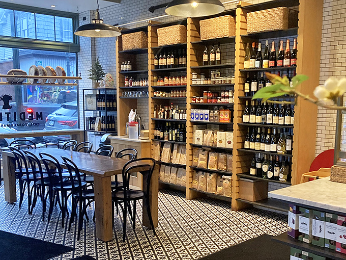 Wine bottles standing at attention like culinary soldiers, ready to complement whatever masterpiece emerges from the kitchen. The communal table whispers, "Stay awhile."