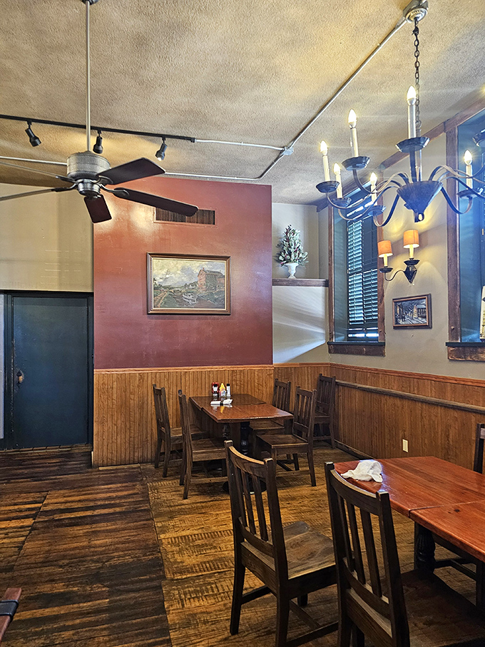 Wooden wainscoting meets burgundy walls in this cozy dining space, where chandeliers cast the kind of glow that makes everyone look like they're having the time of their lives.