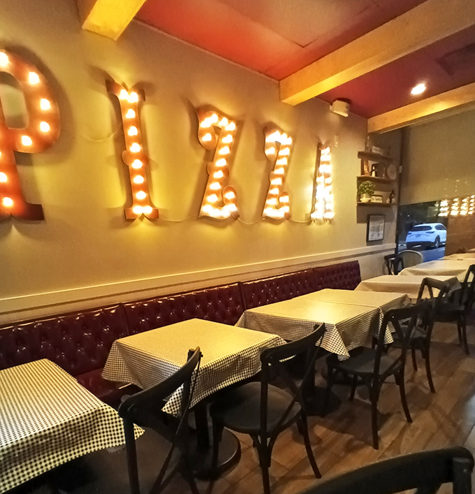 That illuminated "PIZZA" sign isn't just decoration&mdash;it's a promise of deliciousness to come. Classic checkered tablecloths complete the Italian dream.